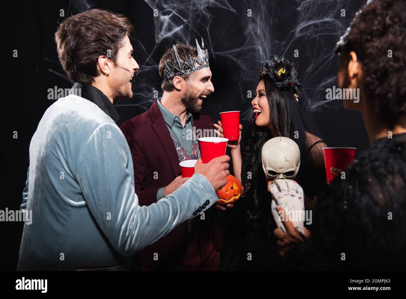 excited multicultural friends in halloween costumes talking during ...