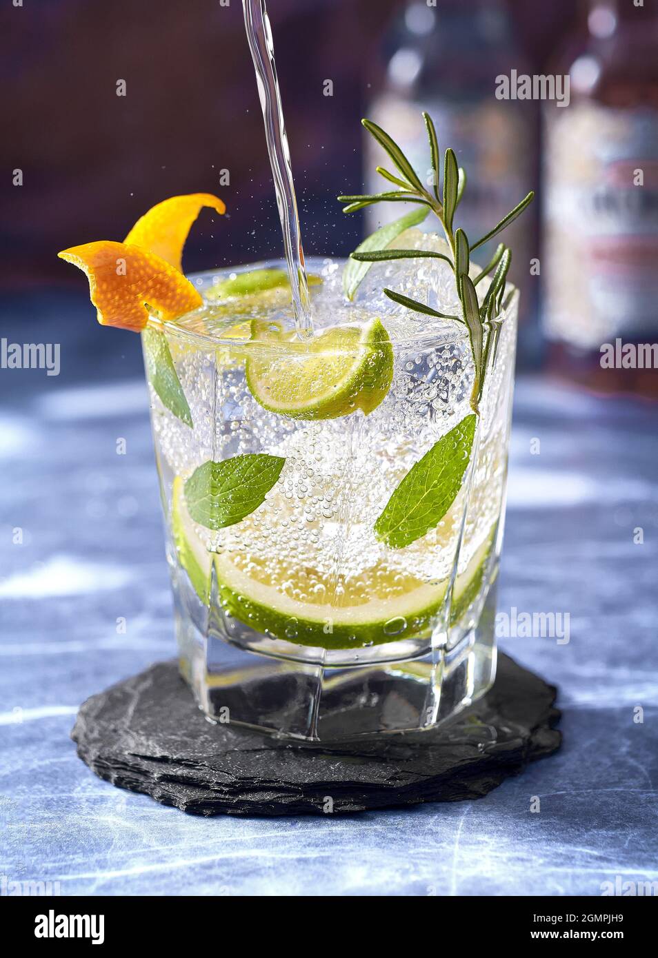 Vertical shot of Gin and Tonic pouring into a glass with rosemary and ...