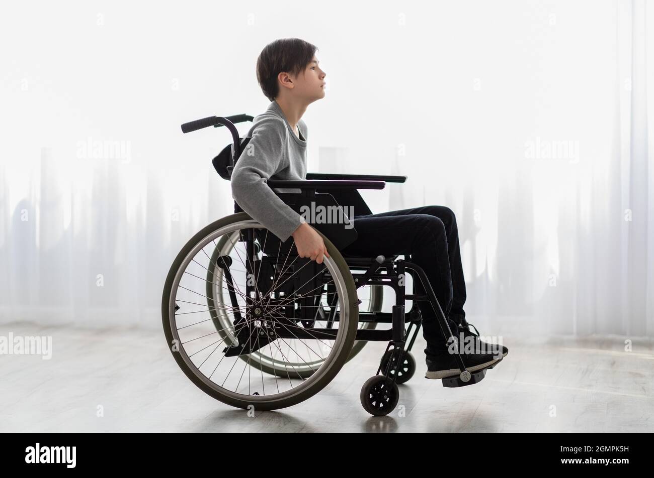 Full length portrait of impaired teenage boy sitting in wheelchair at ...