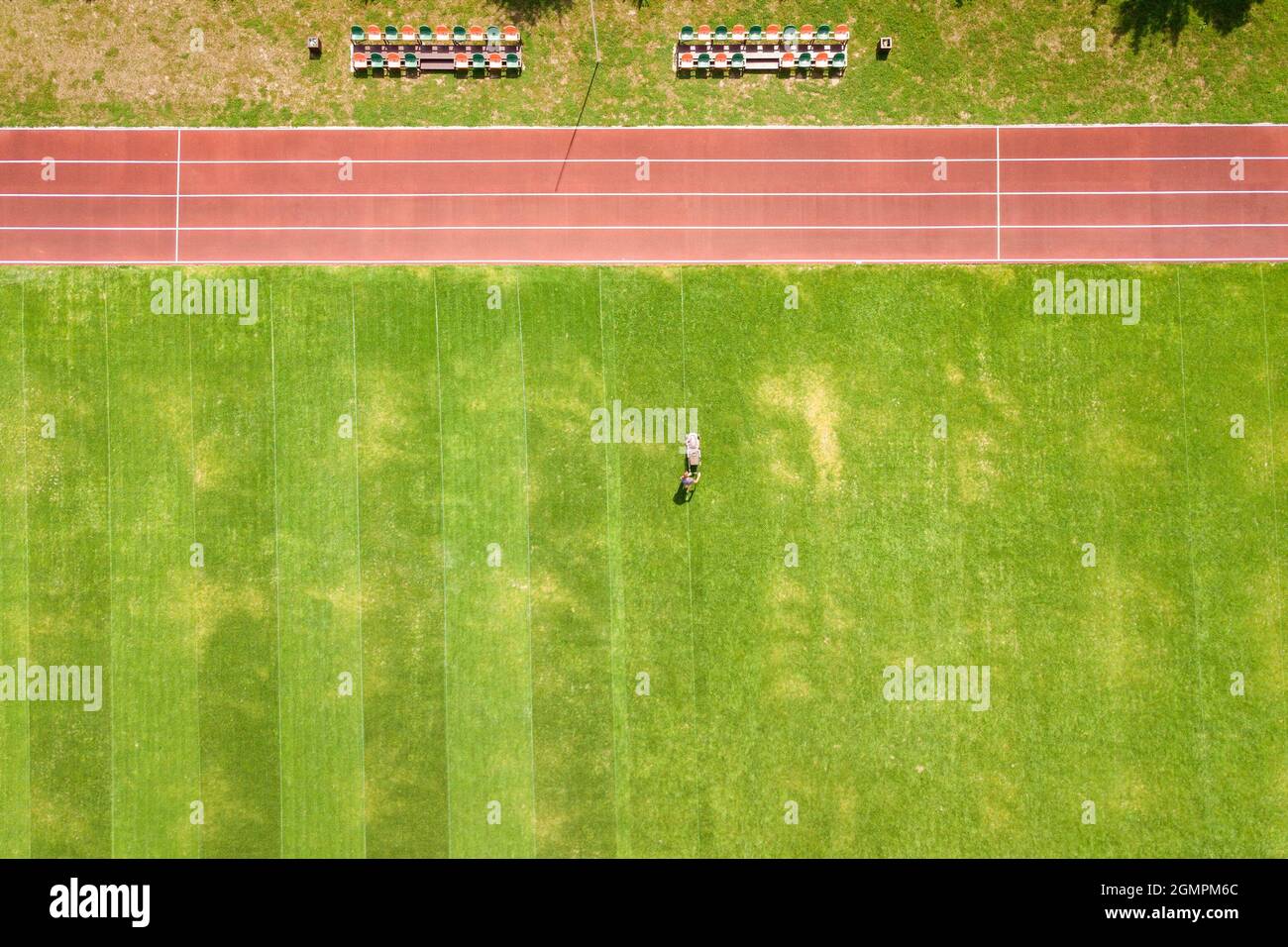 Aerial view of small figure of worker cutting green grass with mowing ...
