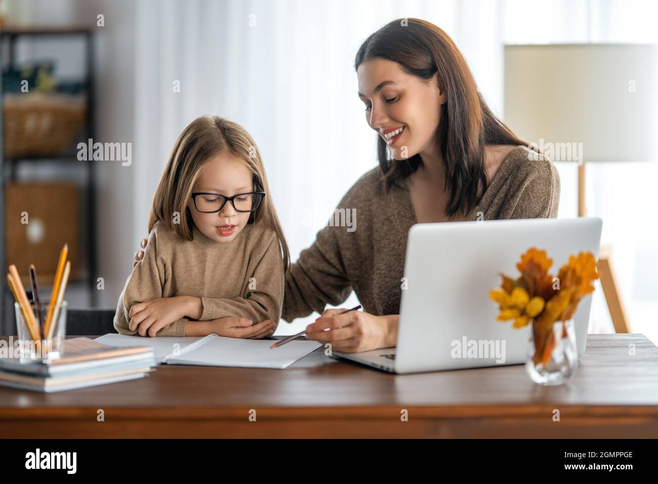Back to school. Happy child and adult are sitting at desk. Girl doing ...