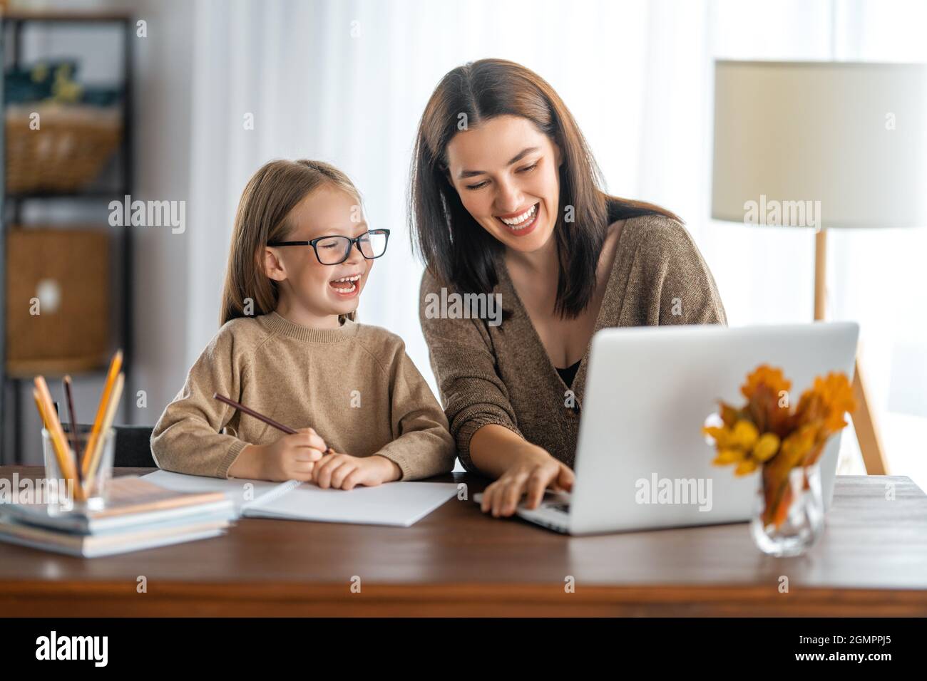 Back to school. Happy child and adult are sitting at desk. Girl doing ...