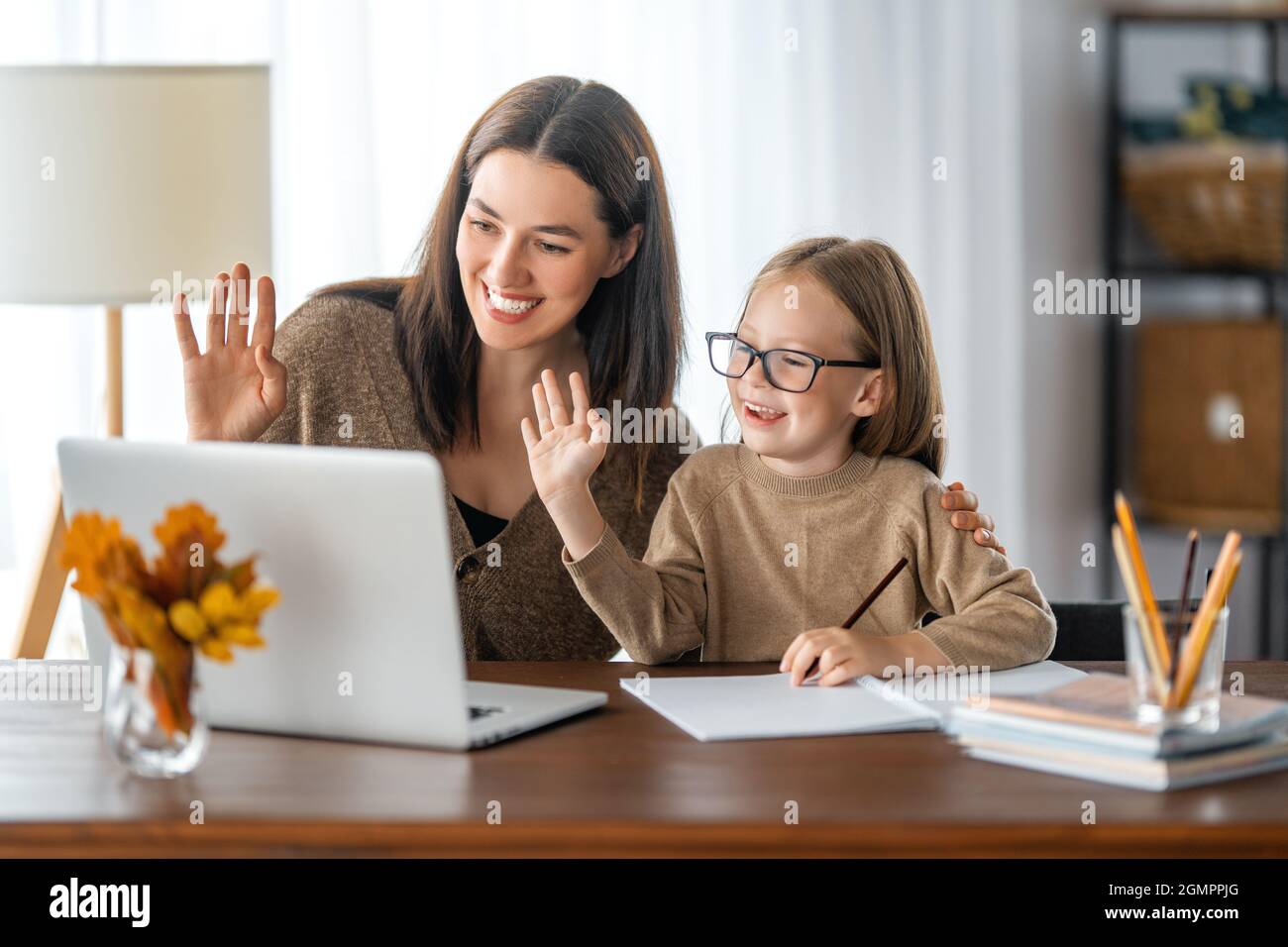 Back to school. Happy child and adult are sitting at desk. Girl doing ...