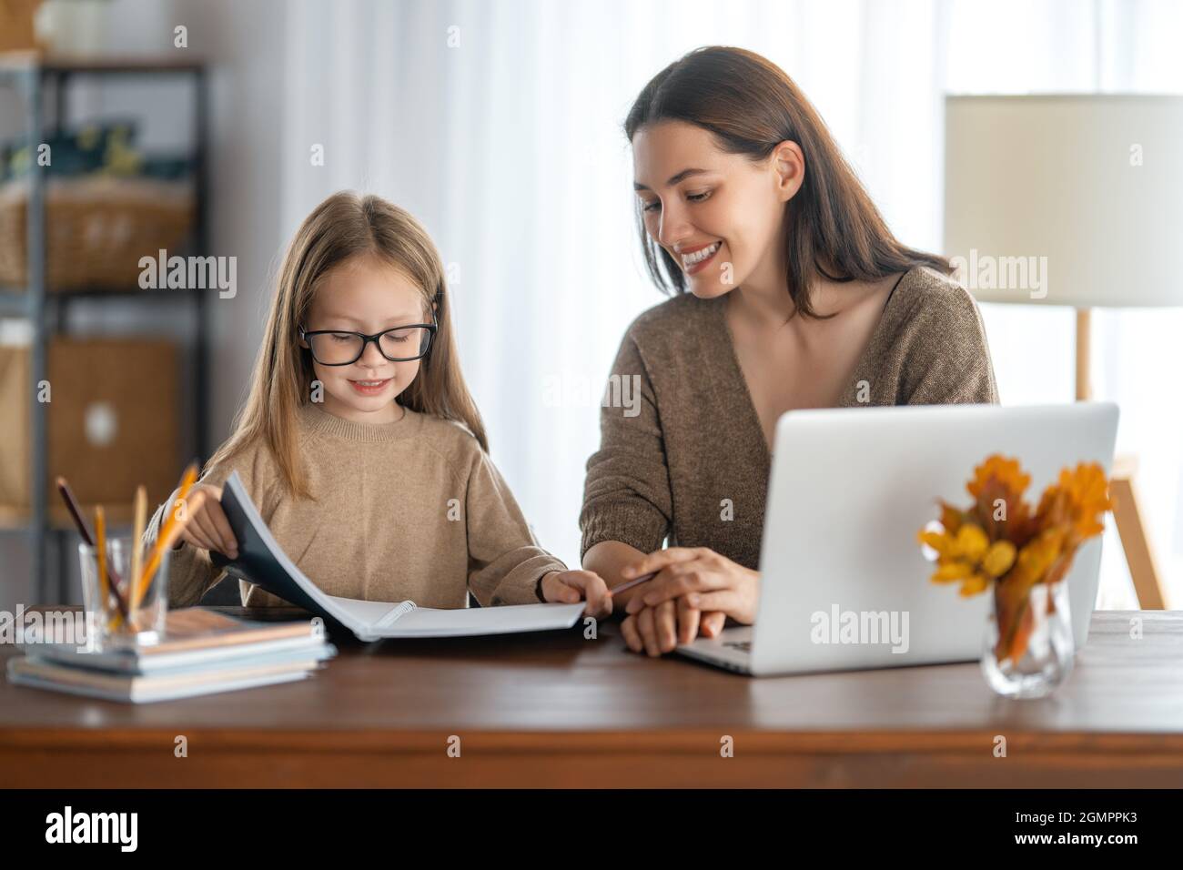 Back to school. Happy child and adult are sitting at desk. Girl doing ...