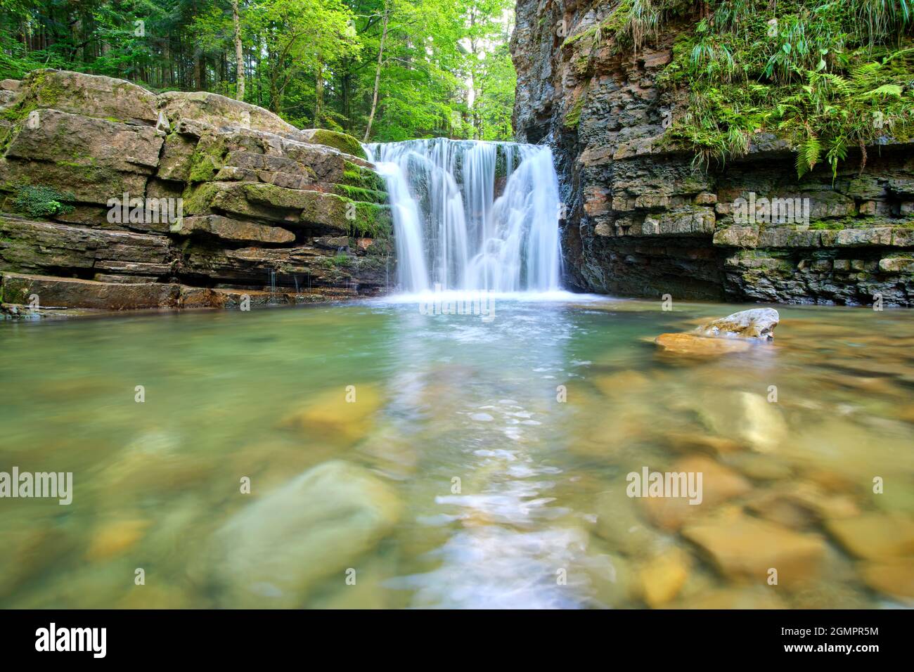 Waterfall on mountain river with white foamy water falling down from rocky formation in summer ...