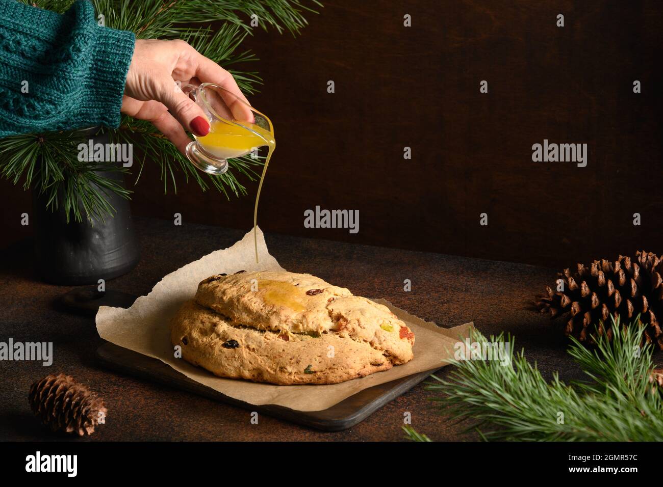 Woman pouring butter on Christmas stollen on a dark brown background ...