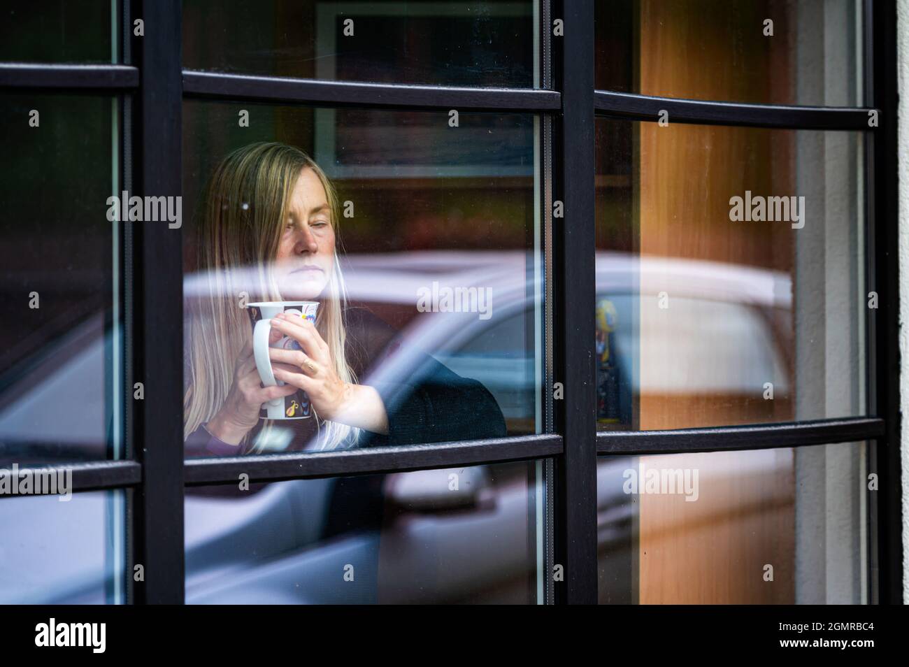 sadly depresive middle aged female looking through the window ...
