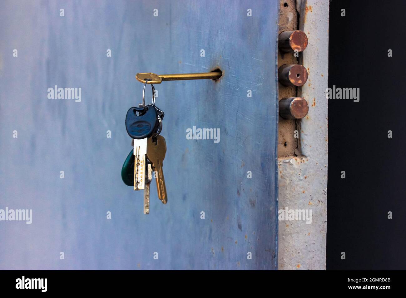 A bunch of chrome keys in a keyhole of a blue-gray metal ajar door. A ...