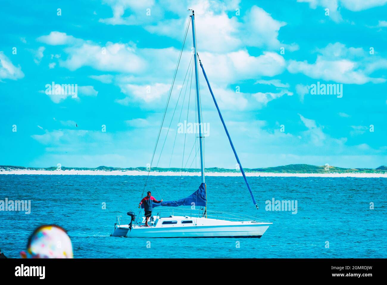 Man on his sailboat with rolled sail at a calm blue sea Stock Photo - Alamy