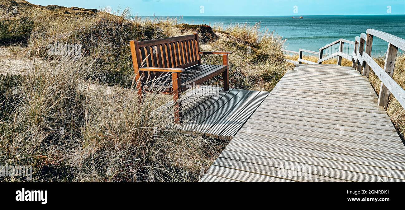 Grassy landscape with a wooden bench on a boardwalk at a coast Stock ...