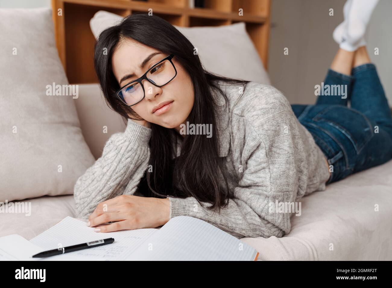 Busy attractive young woman studying while laying on a couch at home ...