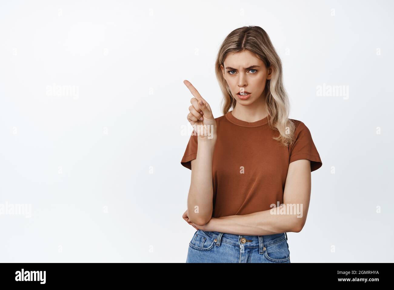 Young angry blond girl pointing finger at upper left corner, furrow ...