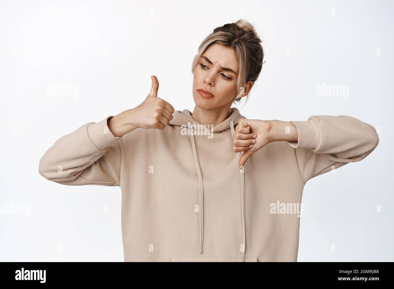 Young woman thinking what feedback leave, showing thumbs up and down ...