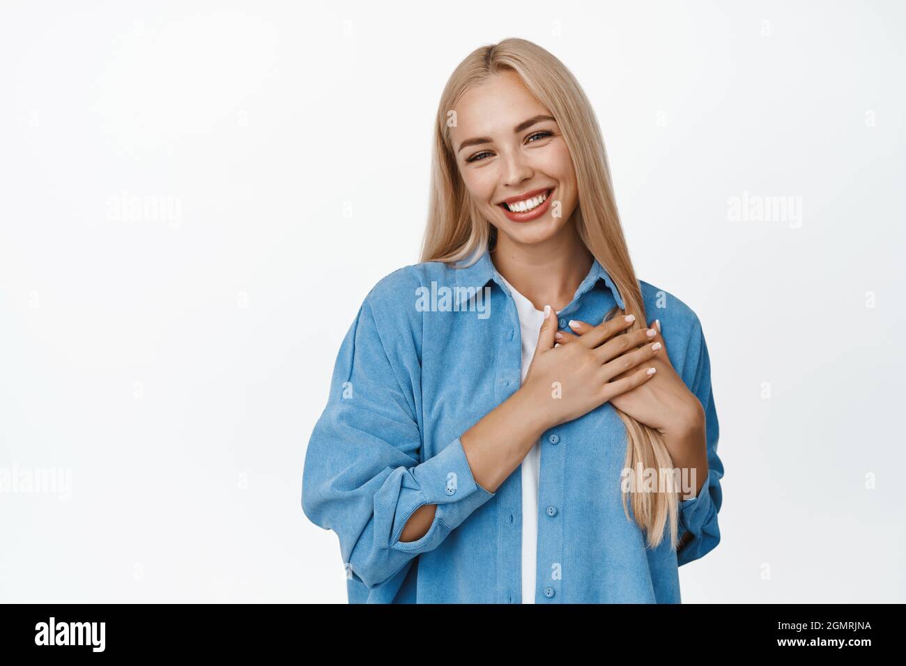 Young Blond Girl Looking Flattered Holding Hands On Heart And Smiling