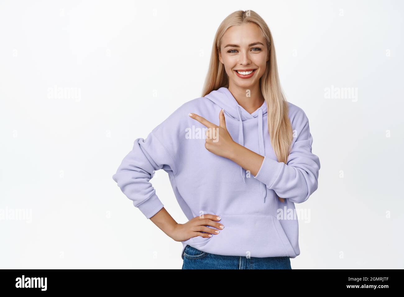 Image of nice and friendly girl smiling, pointing finger at upper left ...