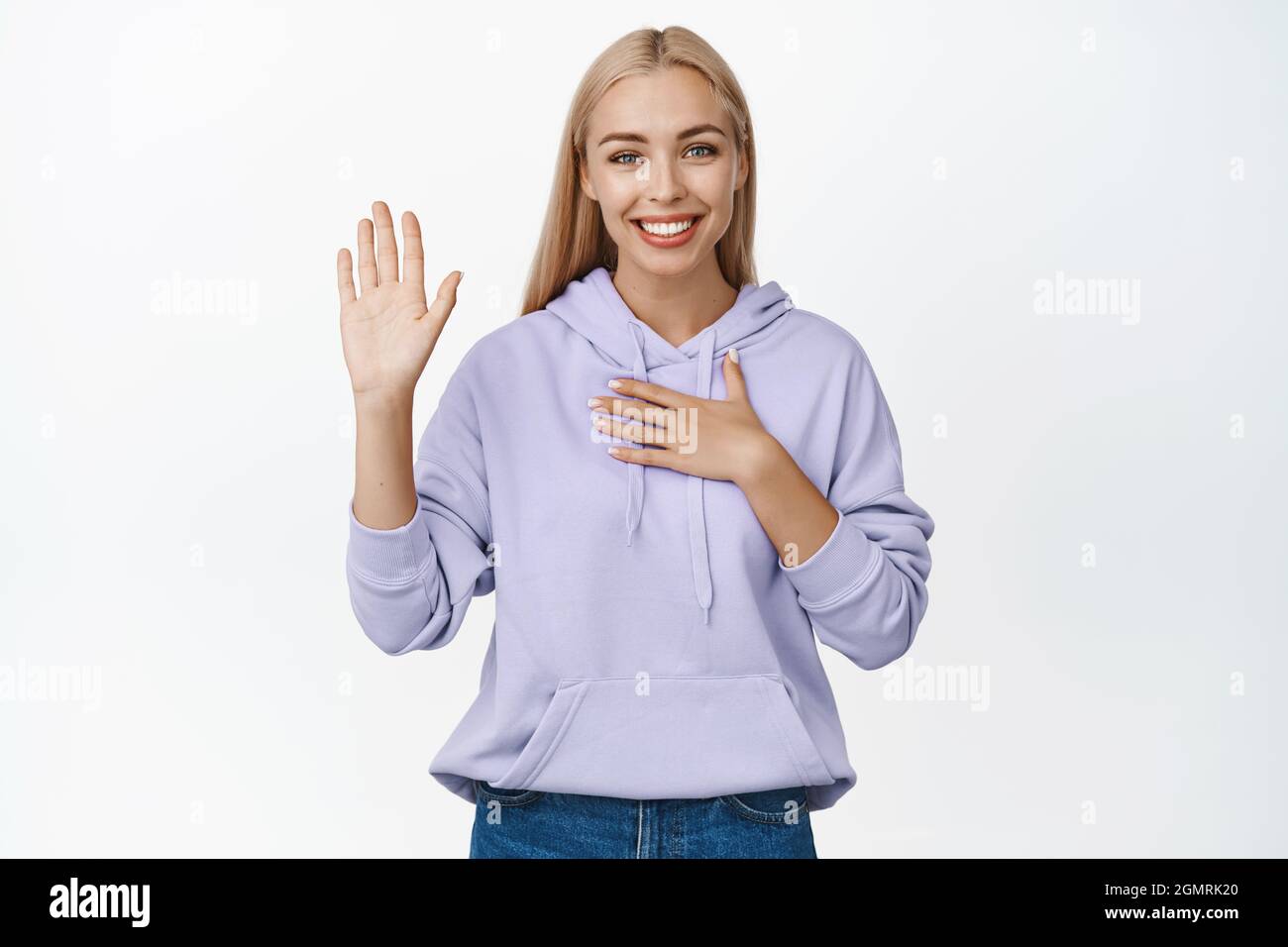 Smiling friendly girl raising hand and put arm on heart, making promise ...