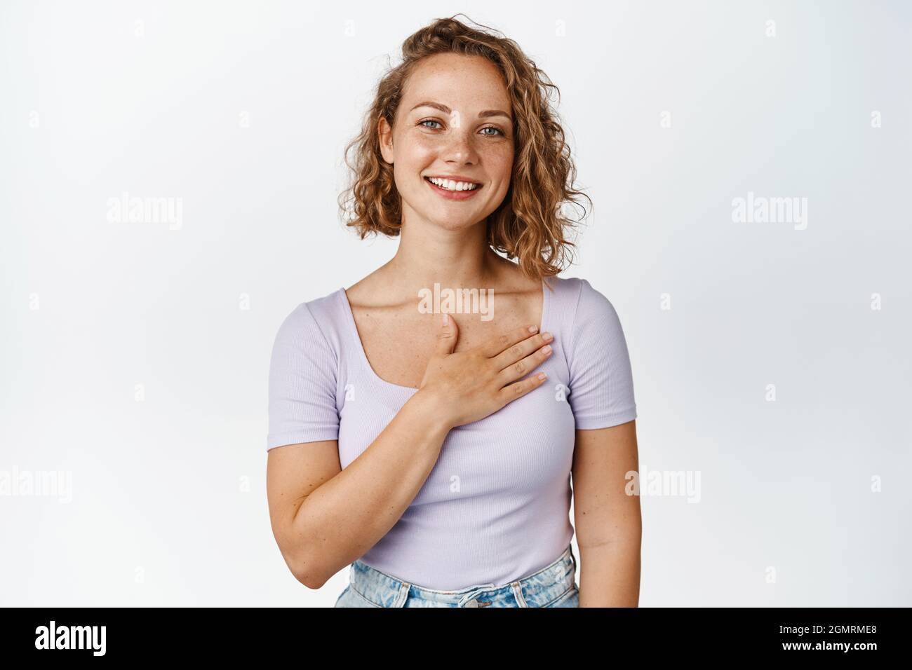 Young Blond Woman Smiling Holding Hand On Heart And Looking Flattered