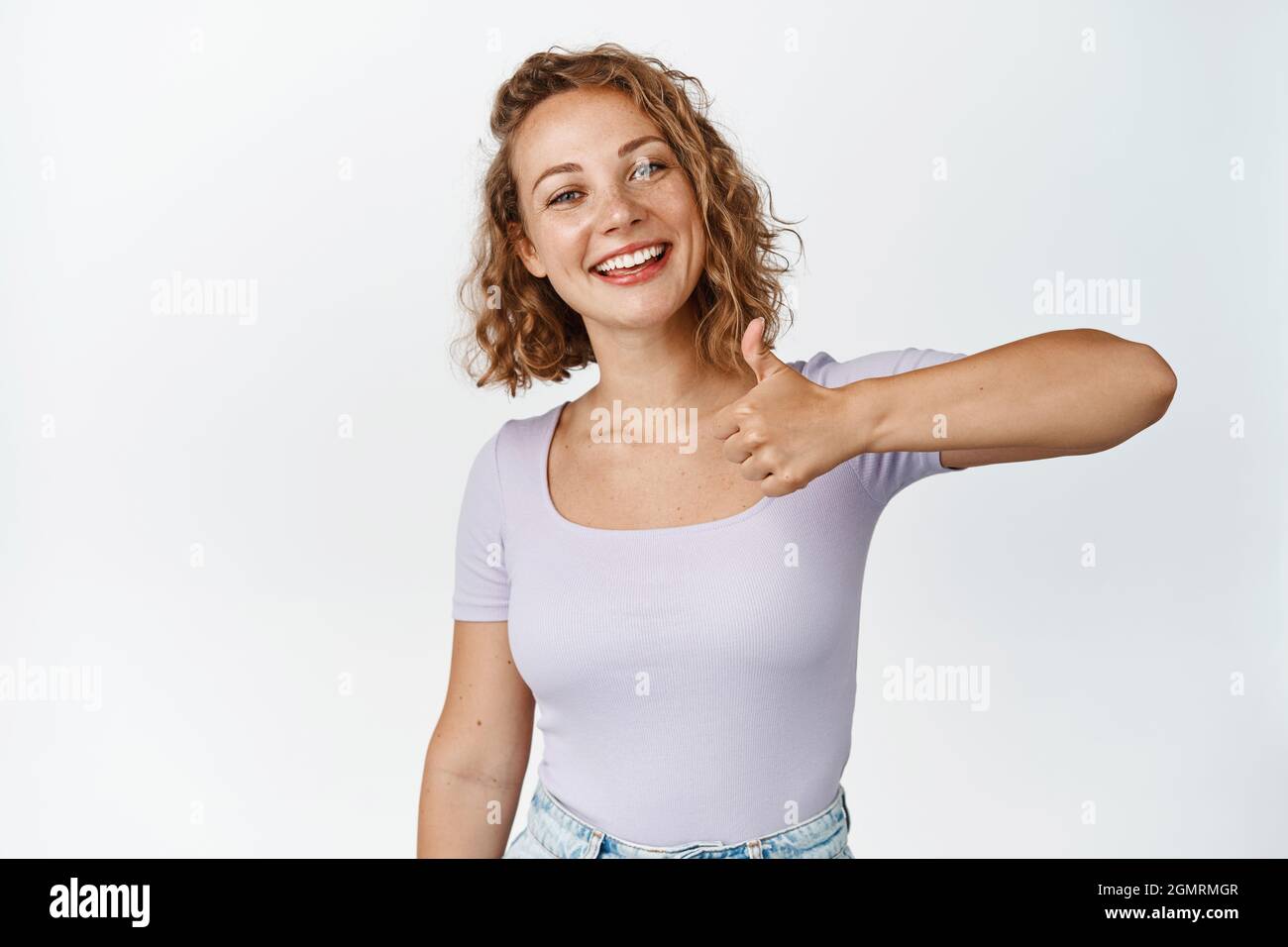 Smiling blond girl shows thumbs up with satisfied face expression ...