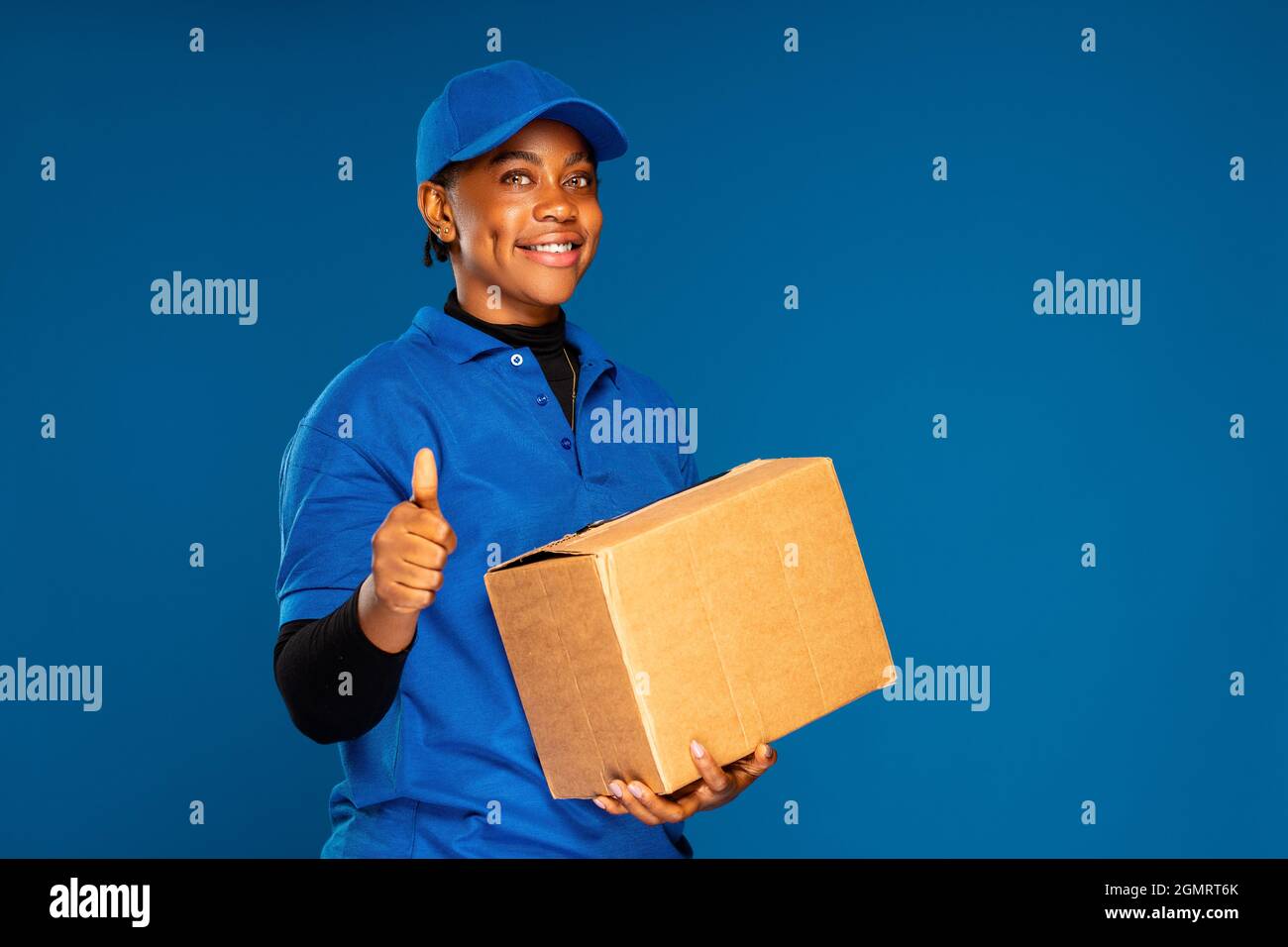 beautiful black female courier worker holding a box, does a thumbs up ...