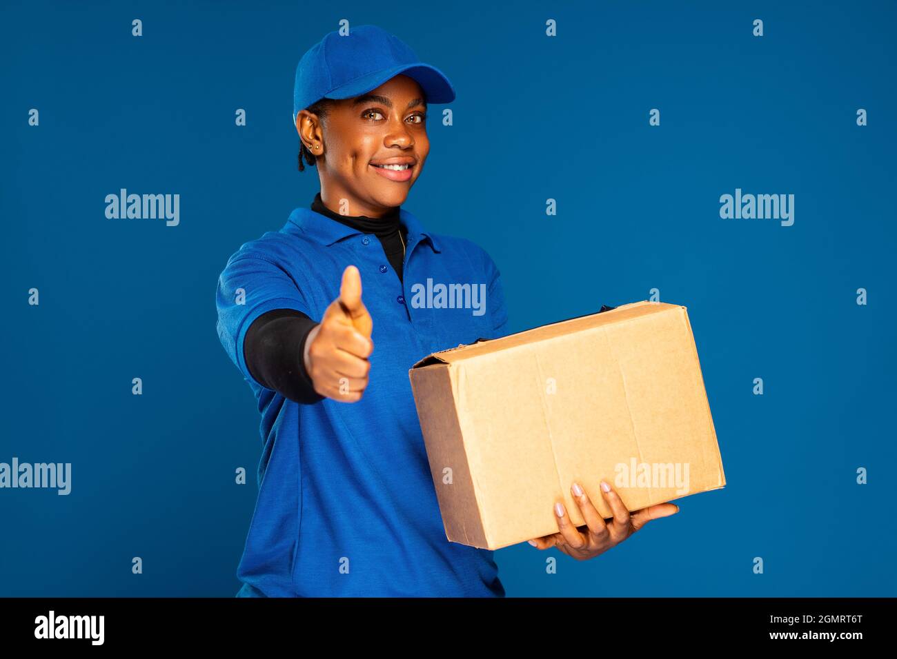 beautiful african female courier worker holding a box, does a thumbs up ...