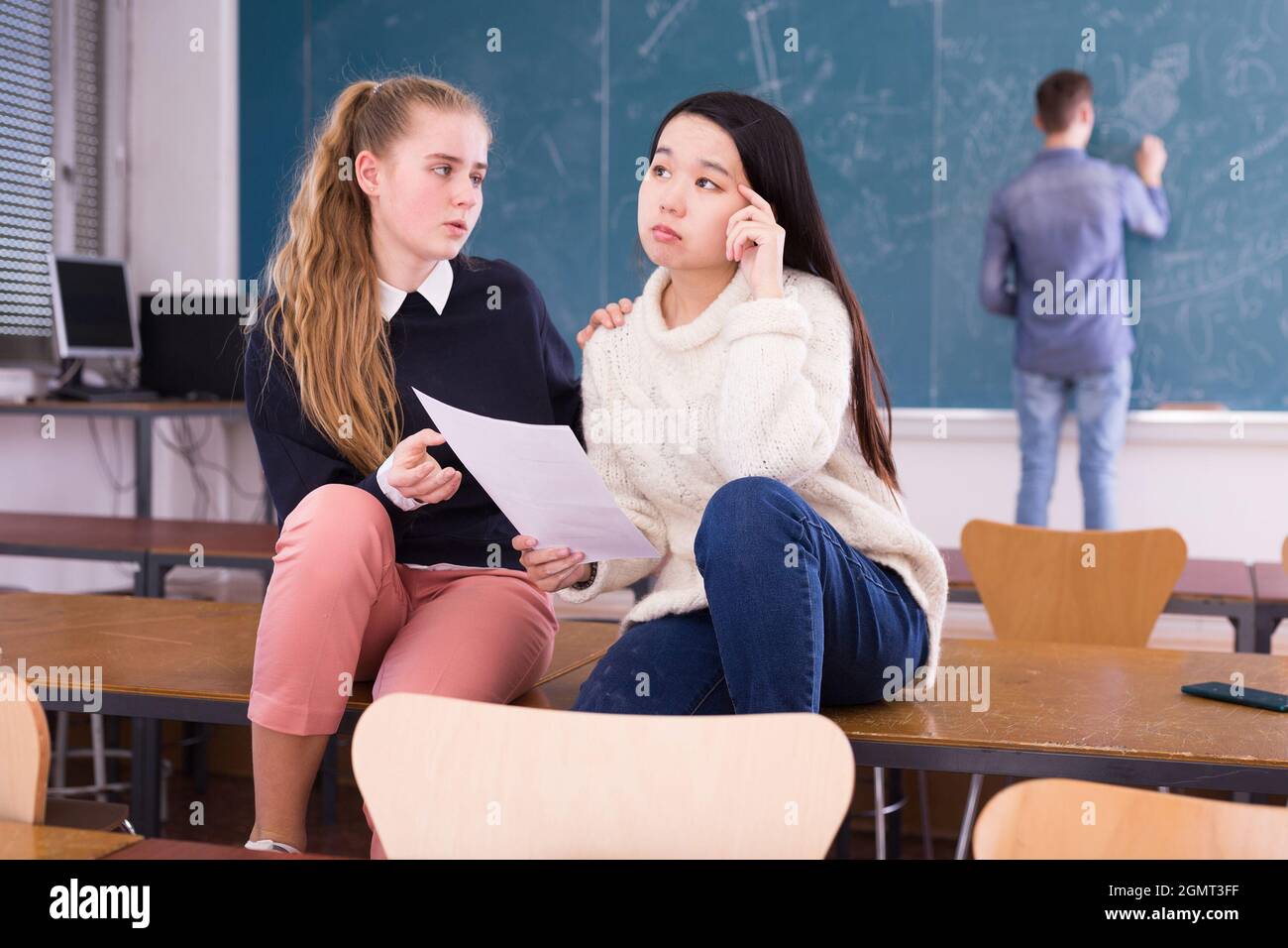 Teen female student supporting upset Chinese girl in classroom Stock ...