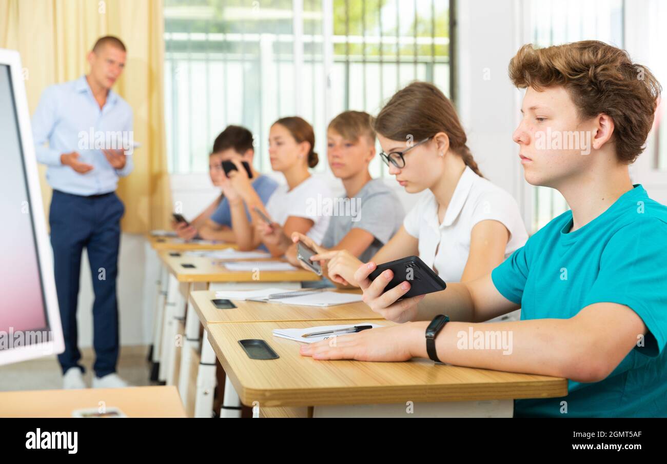 Group of modern teenagers sitting with mobile phones on lesson Stock ...