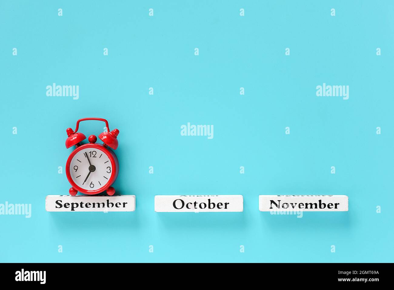 Wooden calendar autumn months and red alarm clock over September on ...