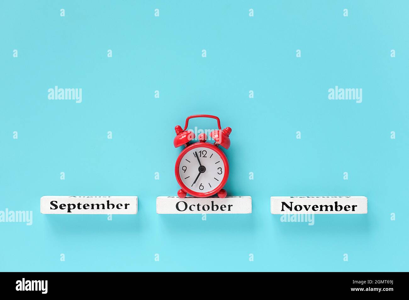 Wooden calendar autumn months and red alarm clock over October on blue ...