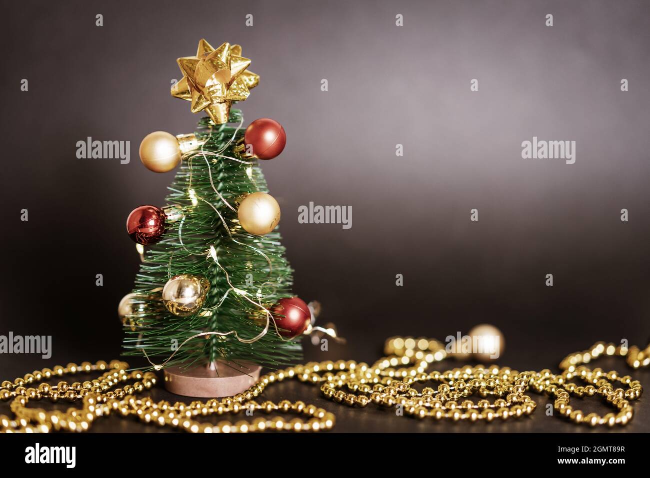 Small decorative christmas tree with toys and a garland on a black background with bokeh ...