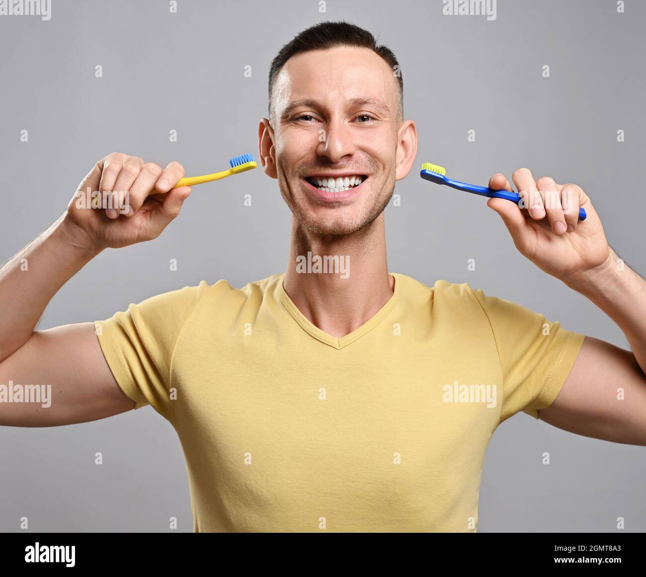 Wide smiling adult man in yellow t-shirt with two toothbrush ...