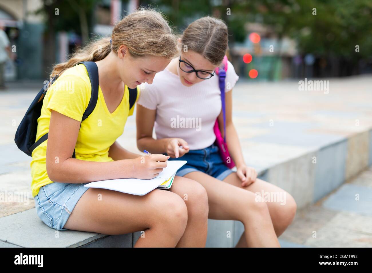 Two happy teenage students studying homework with copybook sitting on parapet outside Stock ...