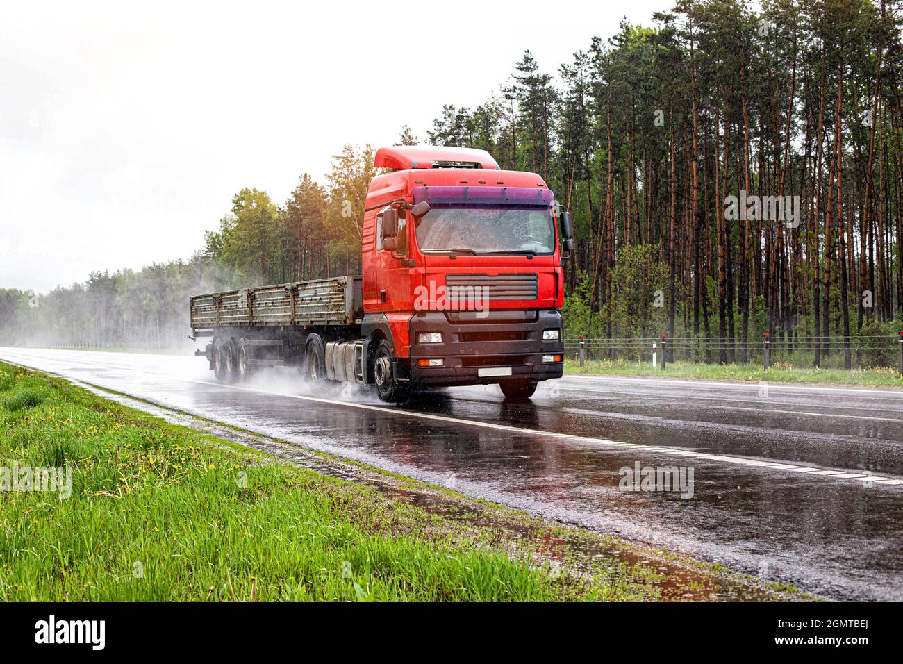 A red flatbed semitrailer tractor driving on the road in rain and poor ...
