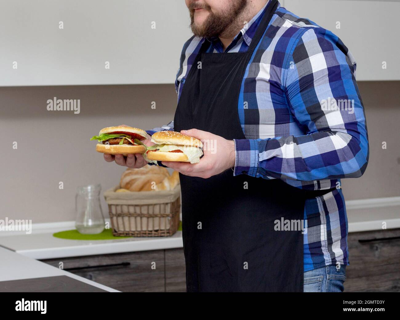 a man with a beard and in an apron holds burgers in his hands in the ...