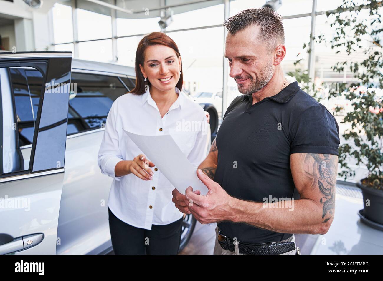 Satisfied client looking at the documents in car dealership Stock Photo ...