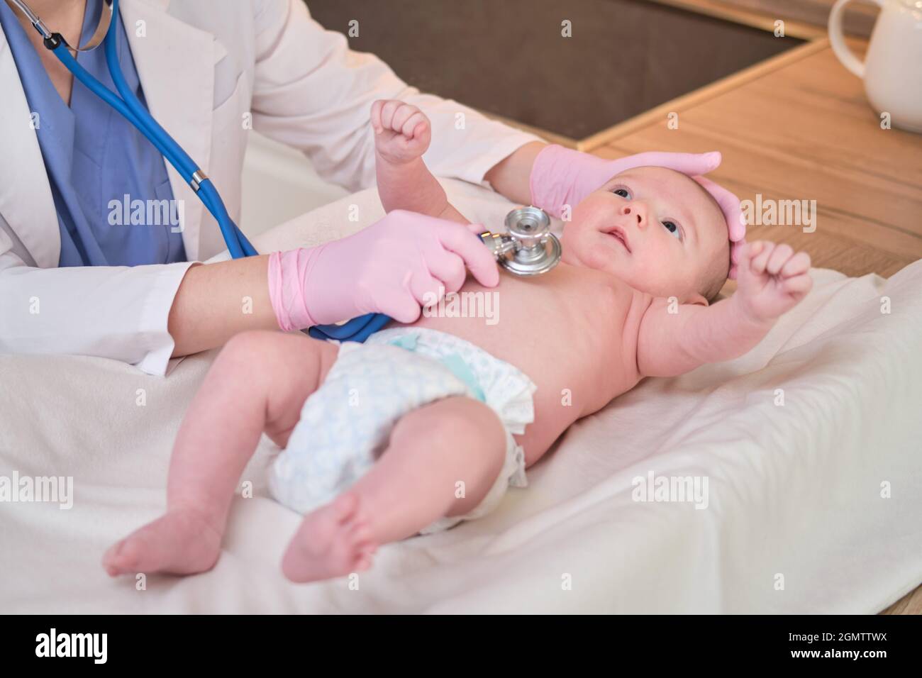 Woman doctor listens with a stethoscope to a newborn baby. Nurse checks ...