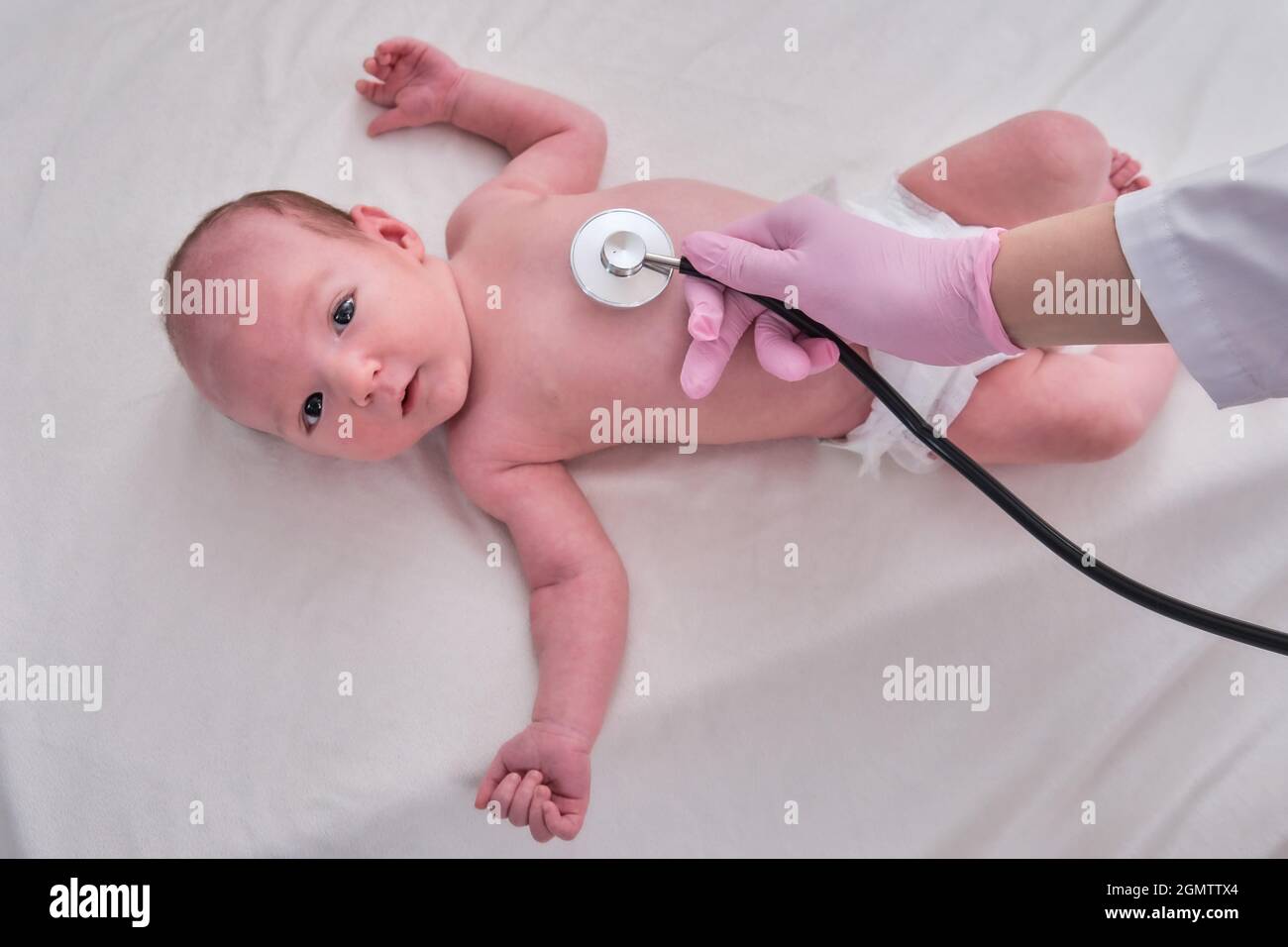 Woman doctor listens with a stethoscope to a newborn baby. Nurse checks ...