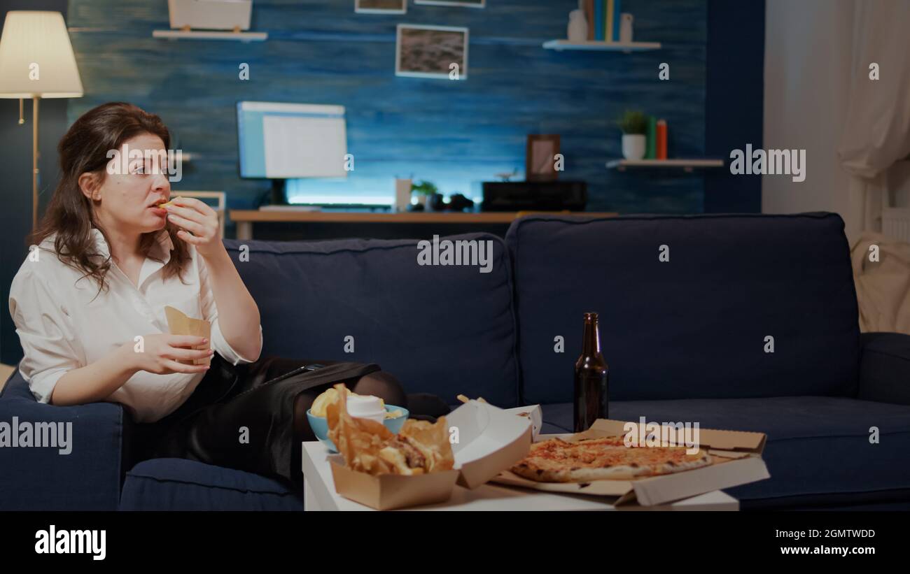 Woman relaxing on couch with takeaway food at home in living room ...