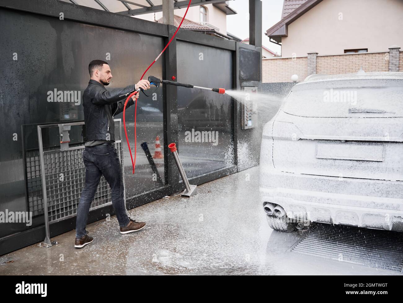 Stylish guy standing at car wash station, holding special gun to apply ...