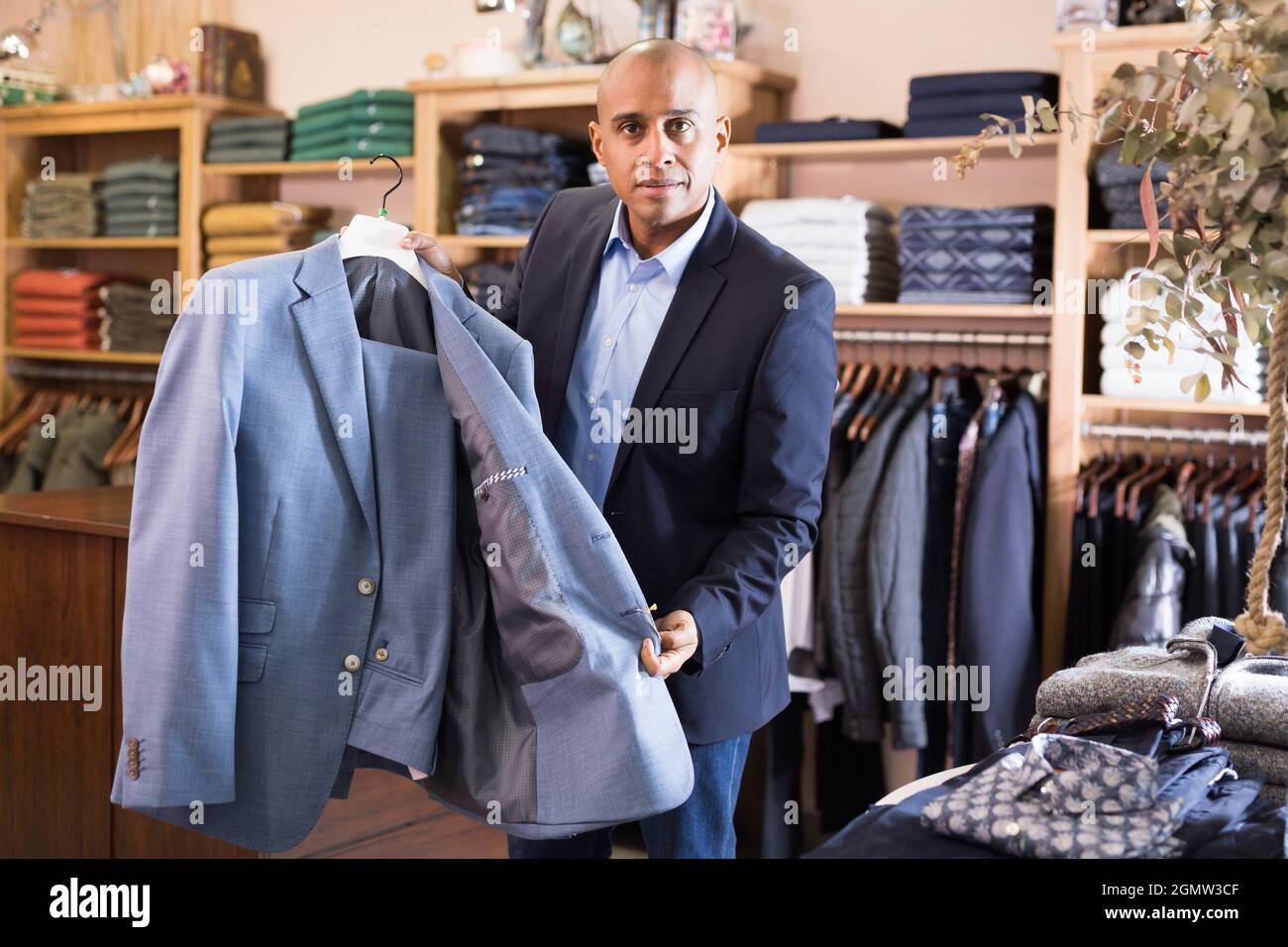 Portrait of confident salesman demonstrating suits in apparel shop ...