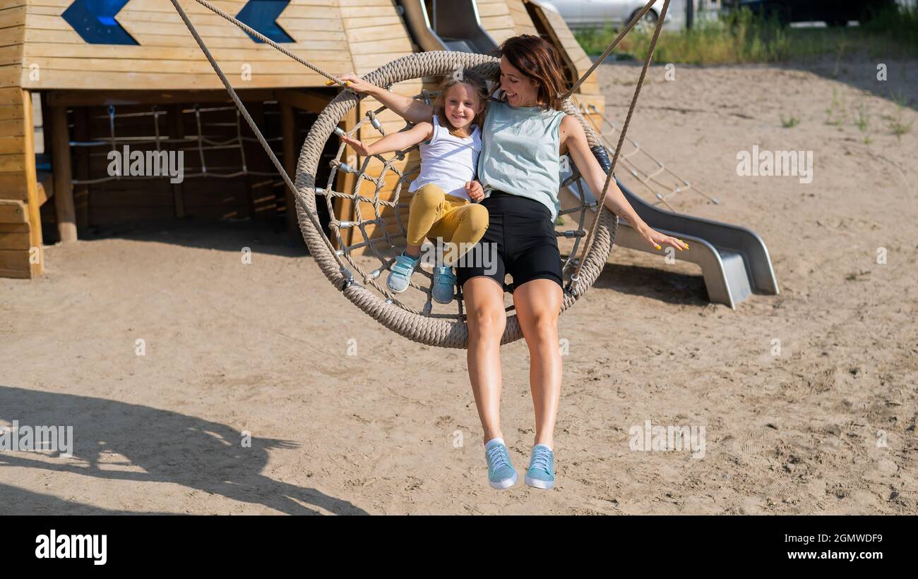 Mom and daughter swing on a round swing. Caucasian woman and little girl have fun on the ...