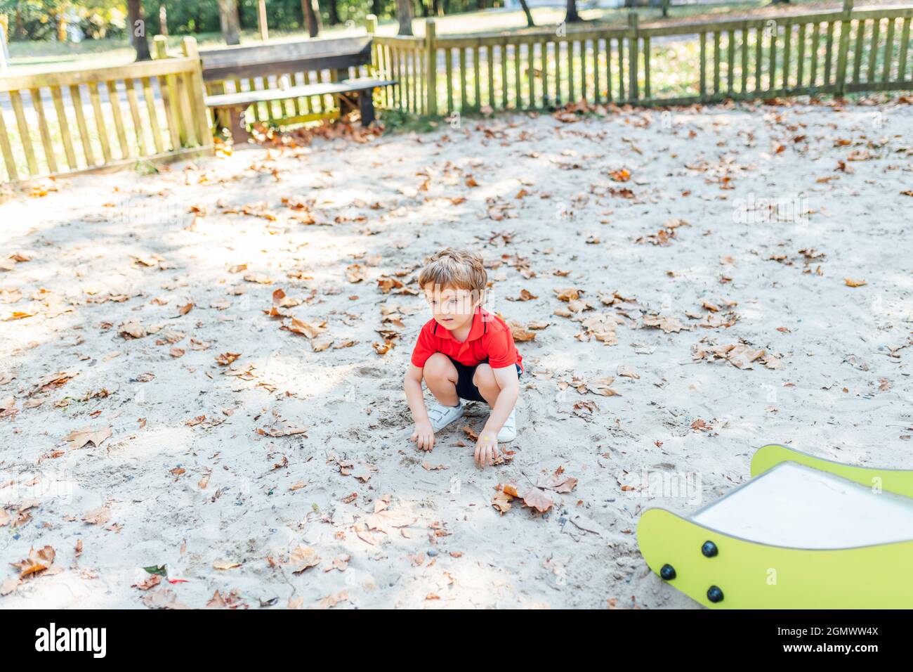 three year old boy sitting squat resting on the sand and dry leaves in ...