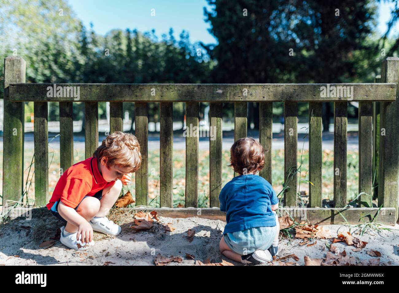 brothers playing on the wooden fence of a playground with the sand and ...