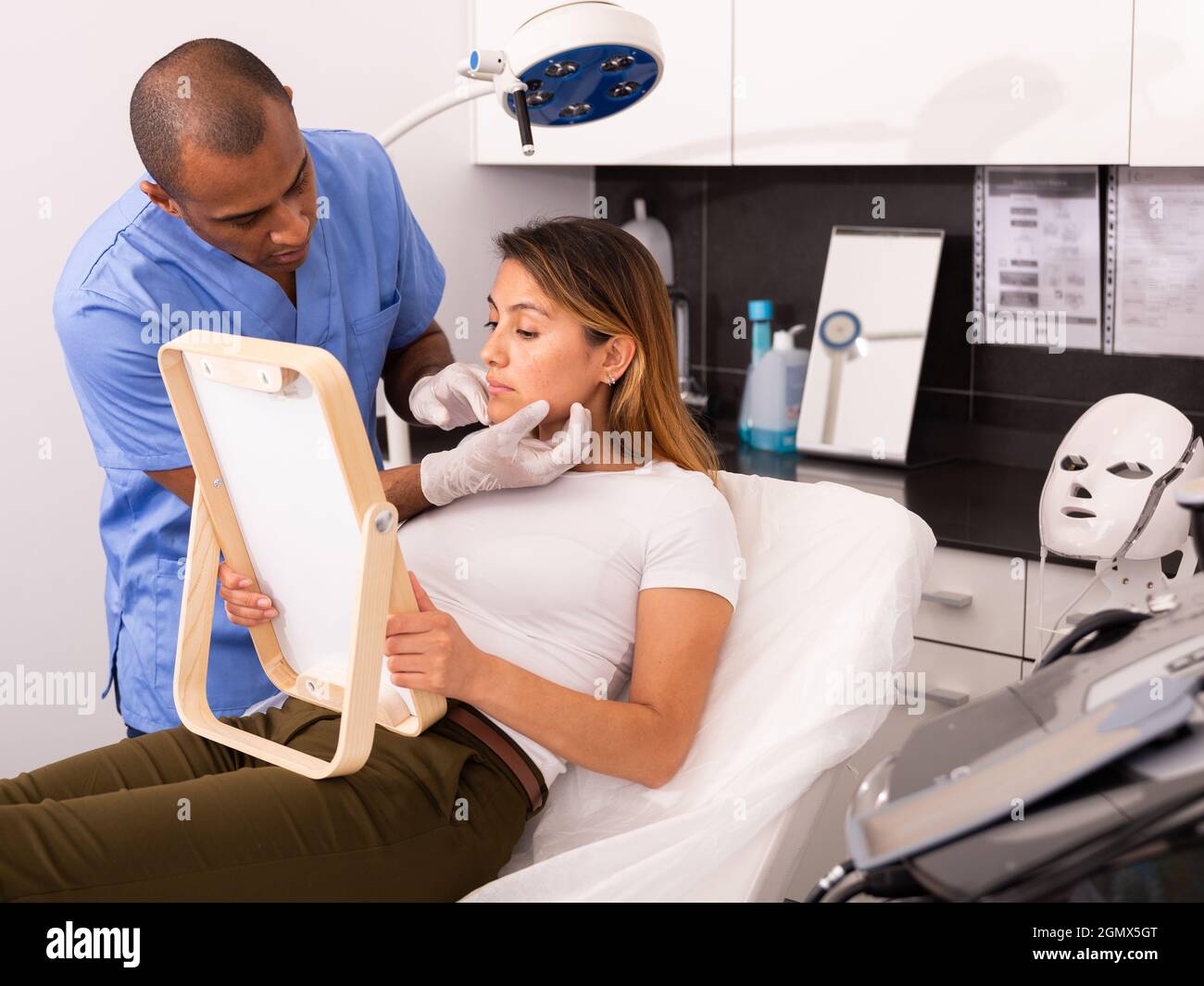 Confident cosmetologist examining female client face before procedure ...