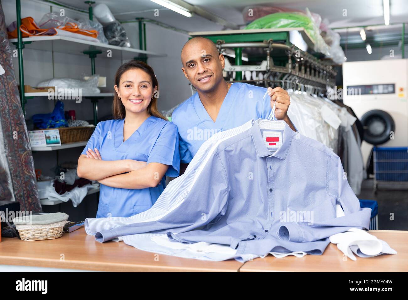Two smiling workers offering professional dry cleaning, showing clean ...