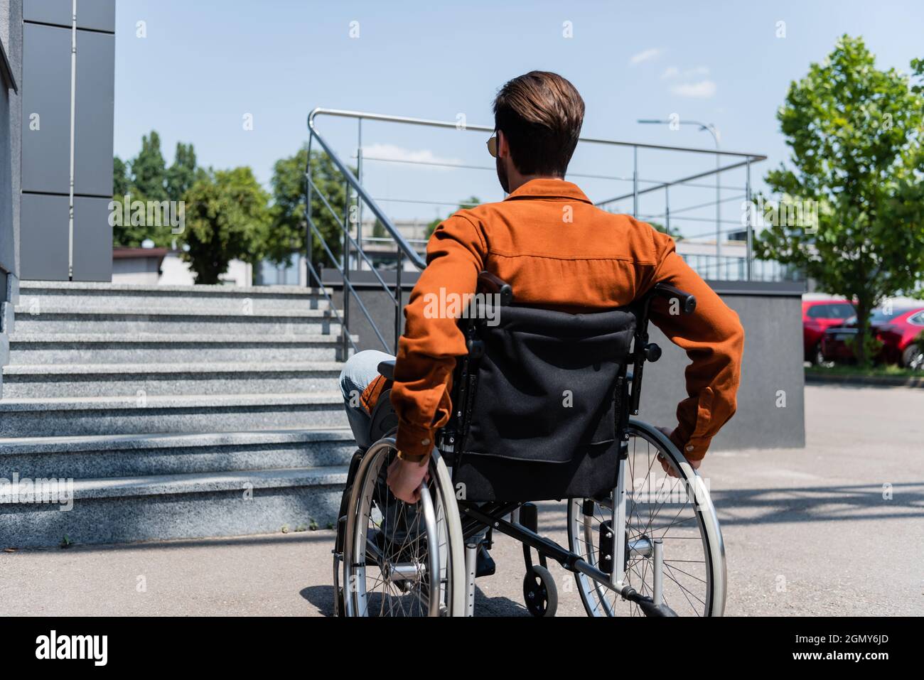 back view of disabled man in wheelchair near stairs on city street ...