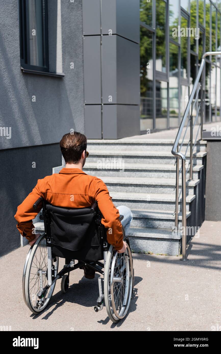 back view of young disabled man in wheelchair near building with stairs ...