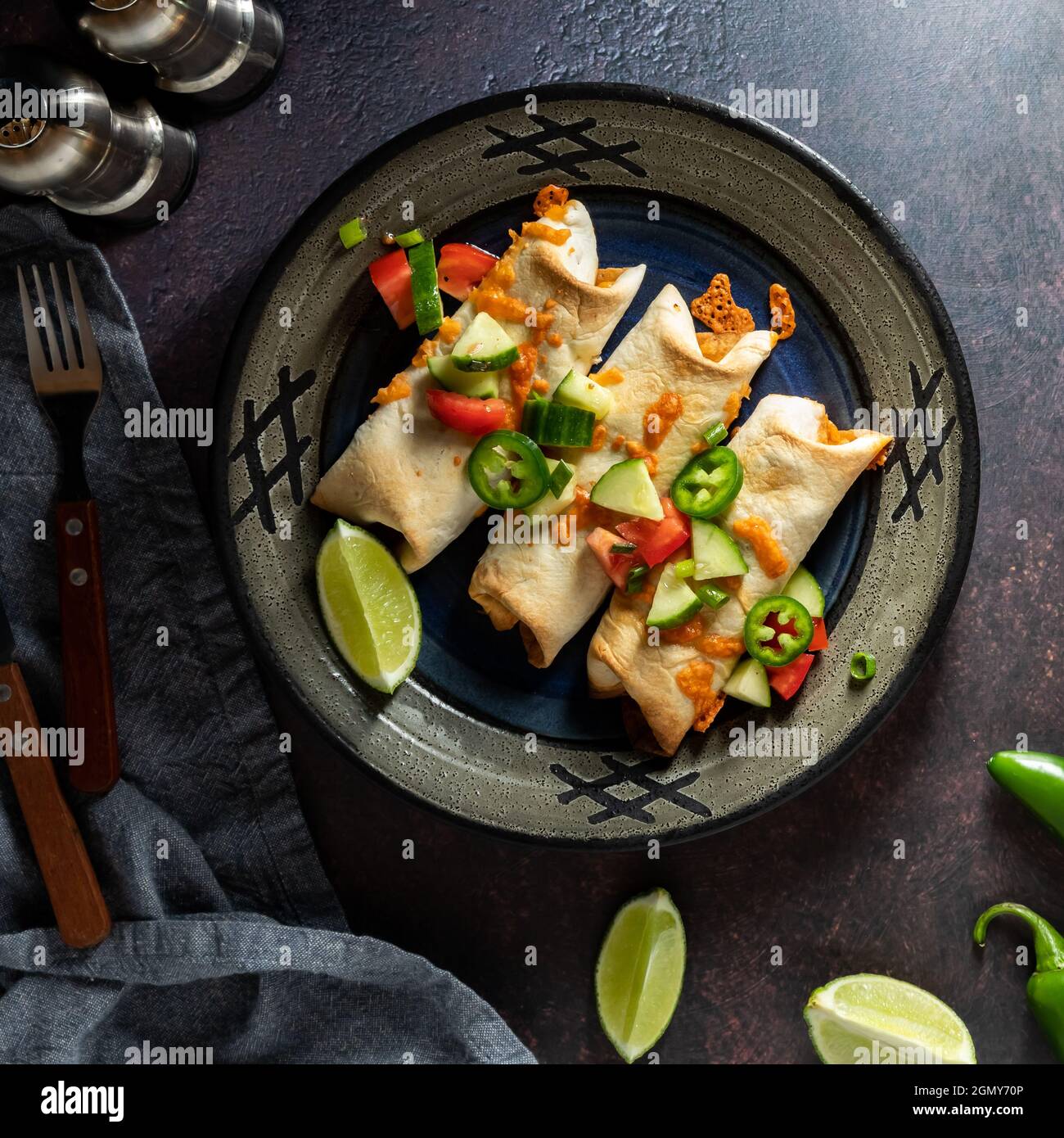Top down view of a plate of taquitos topped with a cucumber and tomato ...