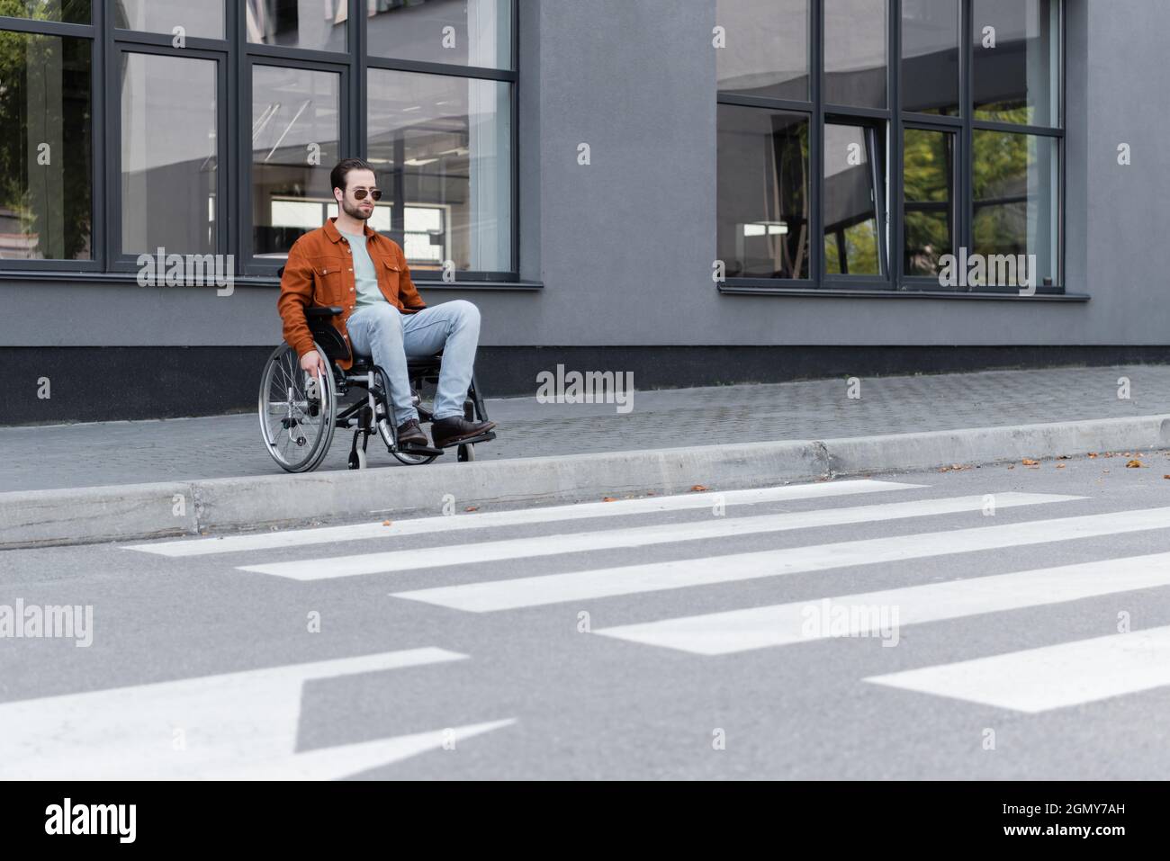 young handicapped man sitting in wheelchair near border and crosswalk ...