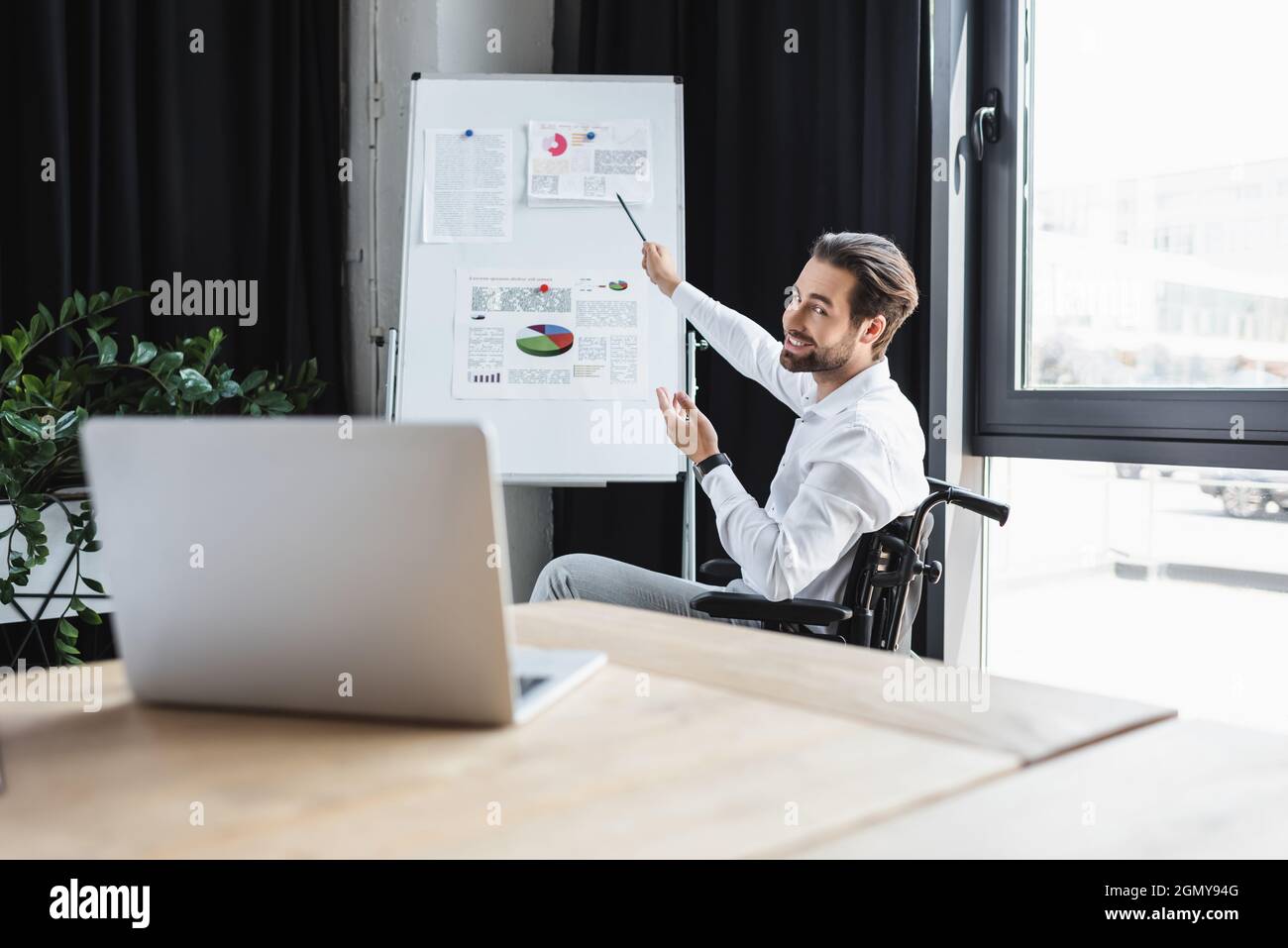 disabled businessman smiling while pointing at flip chart during video ...
