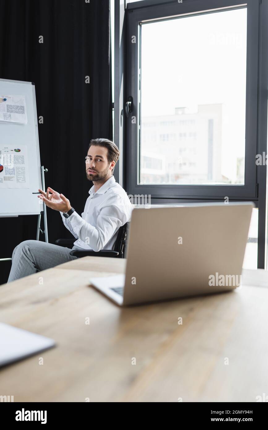 young serious businessman looking at blurred laptop during video call ...